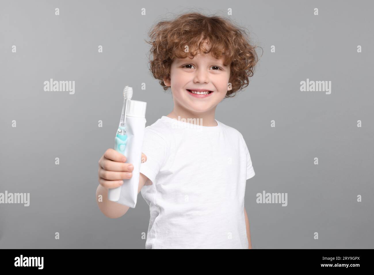 Cute little boy holding electric toothbrush and tube of toothpaste on ...