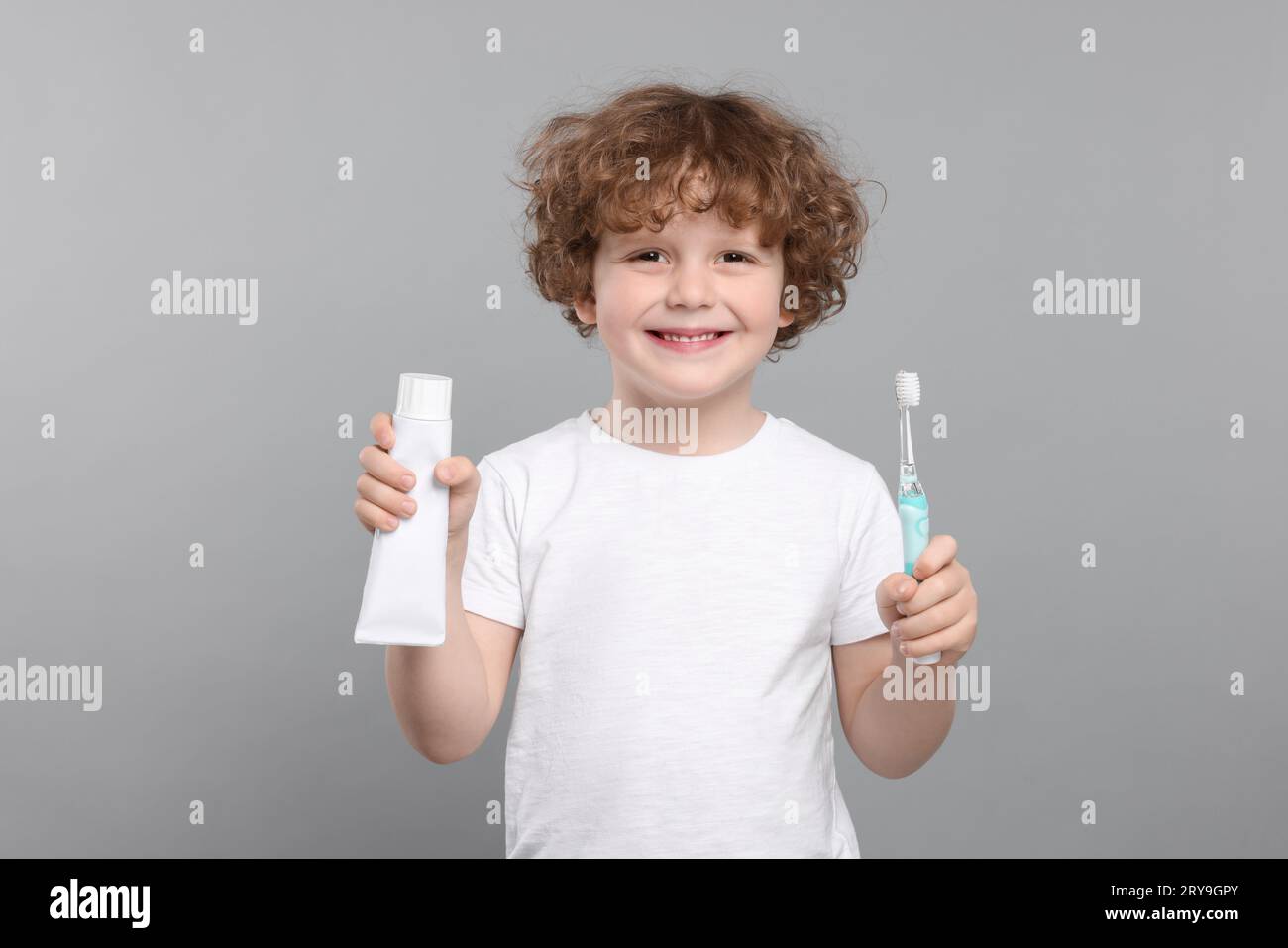Cute little boy holding electric toothbrush and tube of toothpaste on ...