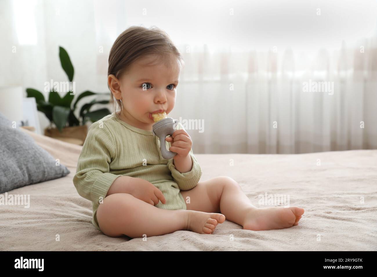 Cute baby girl with nibbler on bed at home. Space for text Stock Photo ...