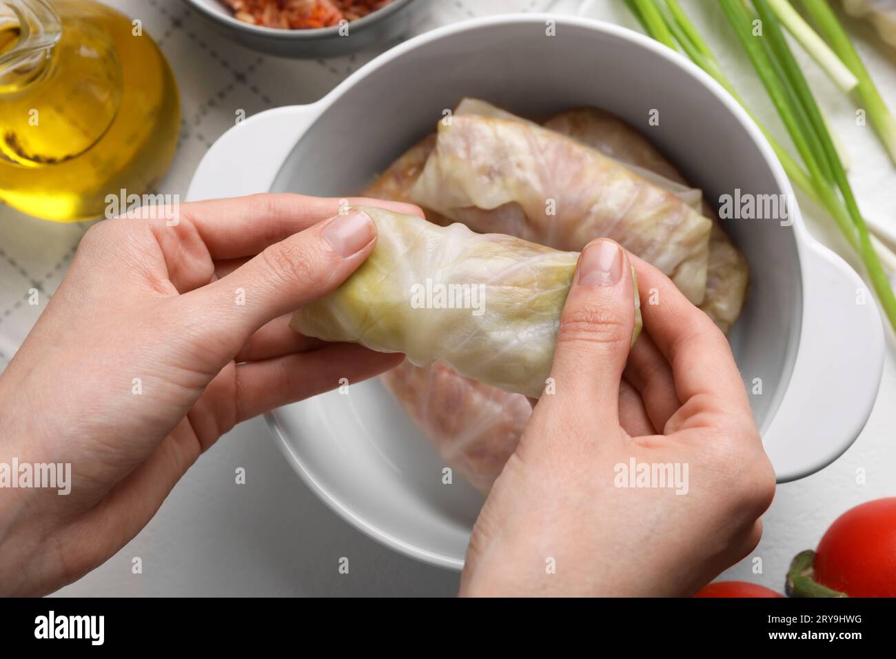 Woman putting uncooked stuffed cabbage roll into ceramic pot at table ...