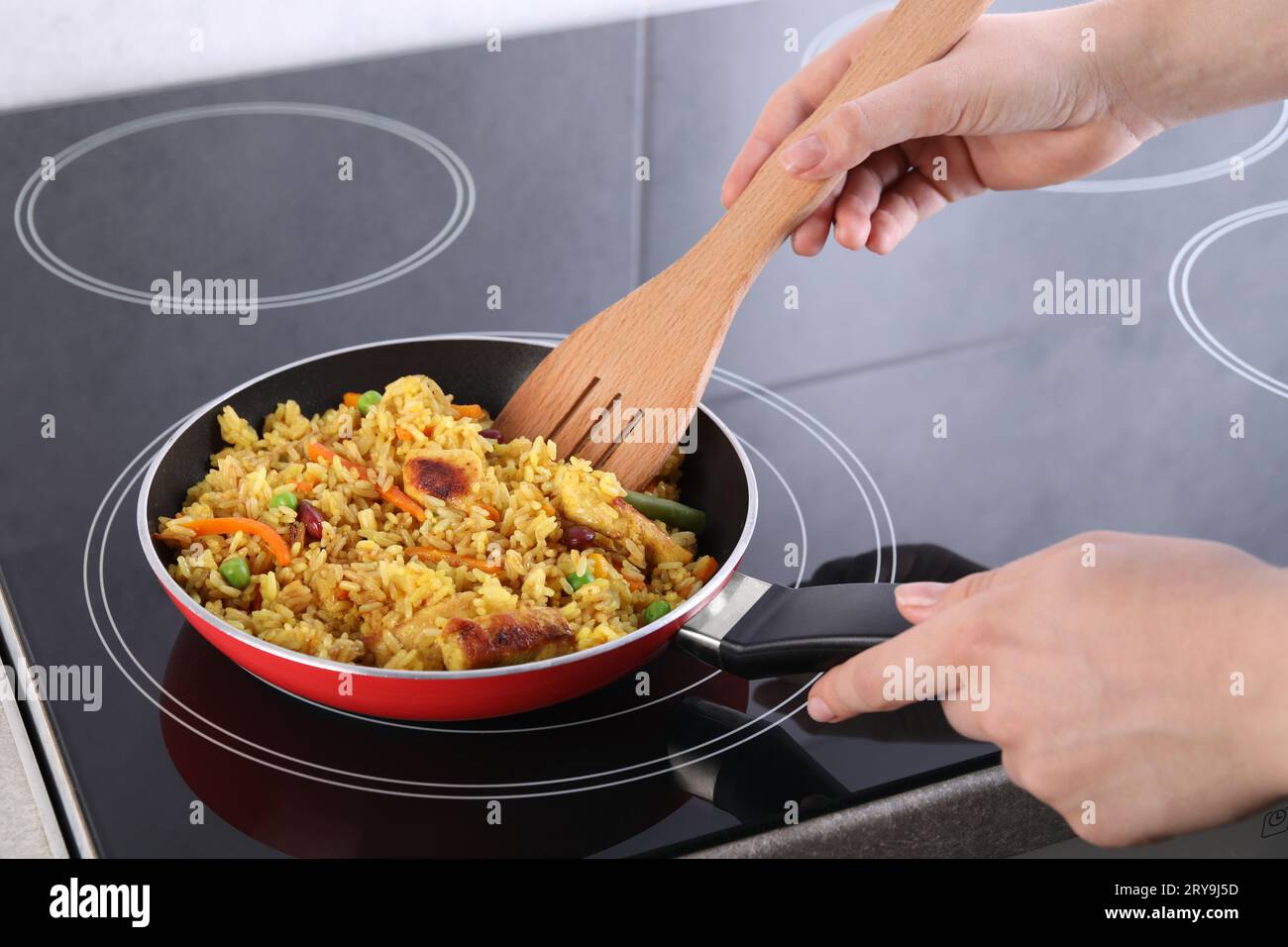 Woman frying rice with meat and vegetables on induction stove, closeup ...