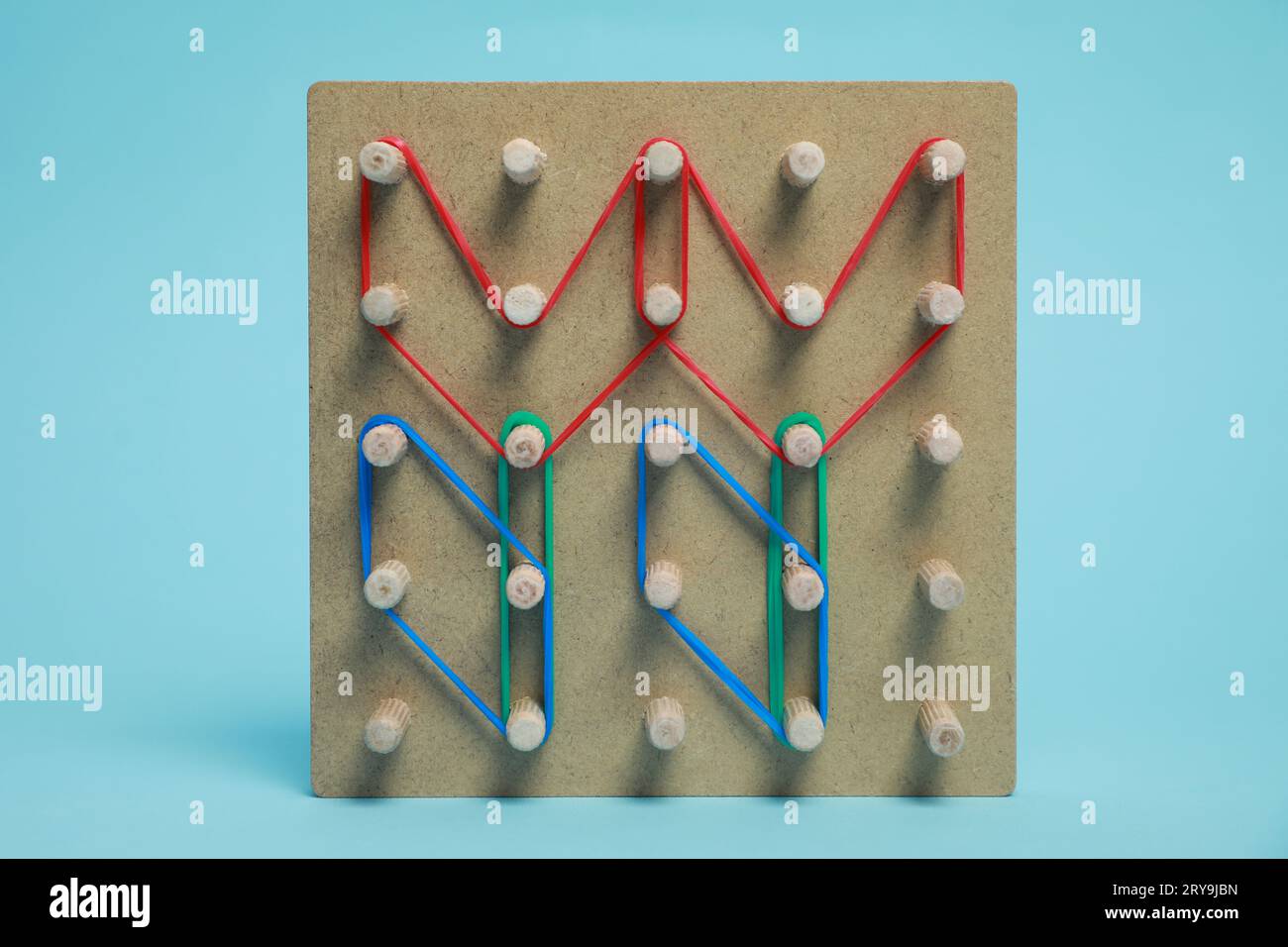 Wooden geoboard with flower shapes made of rubber bands on light blue ...