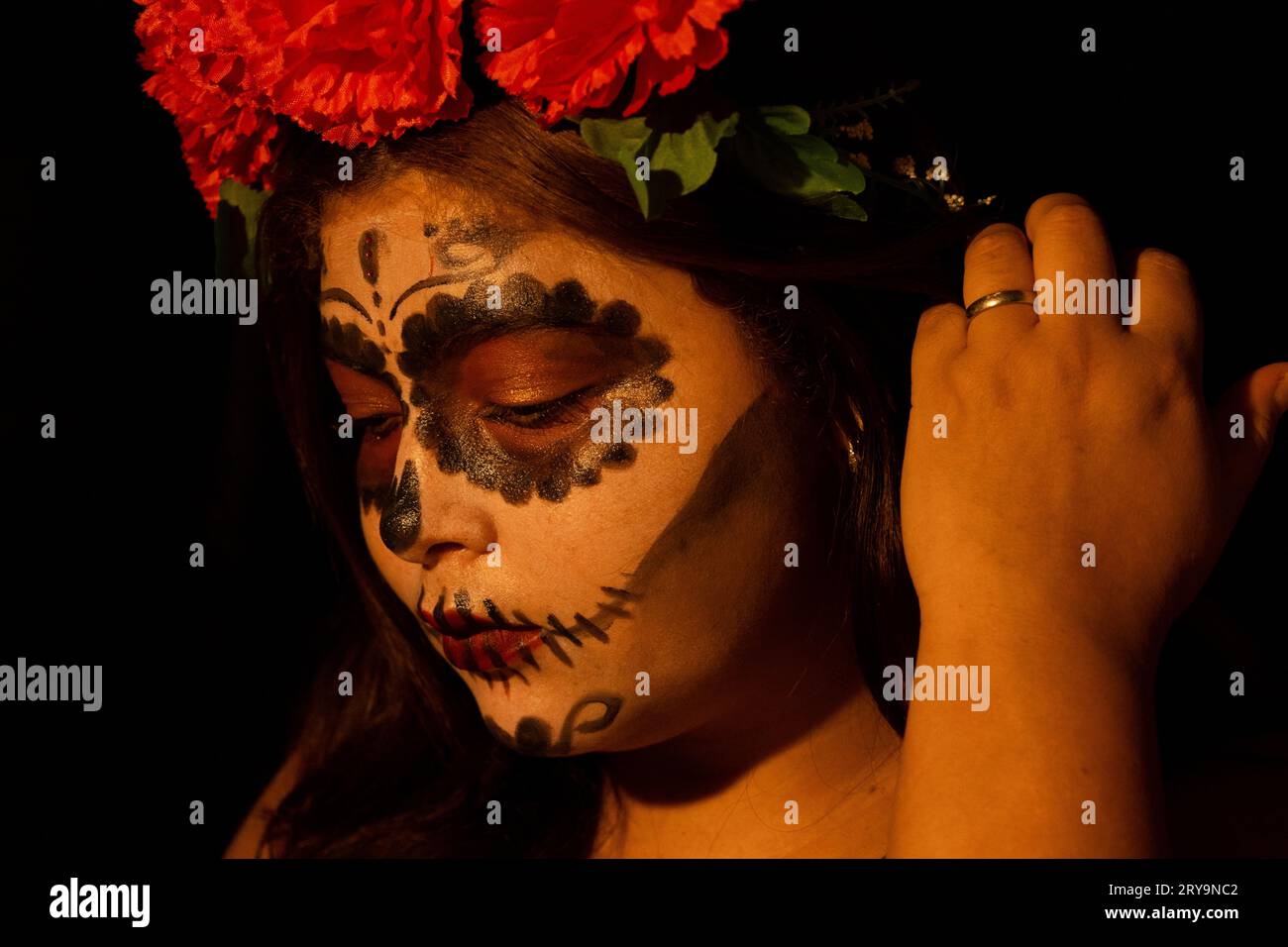 Catrina looking down arranging her hair with red flowers on her head ...