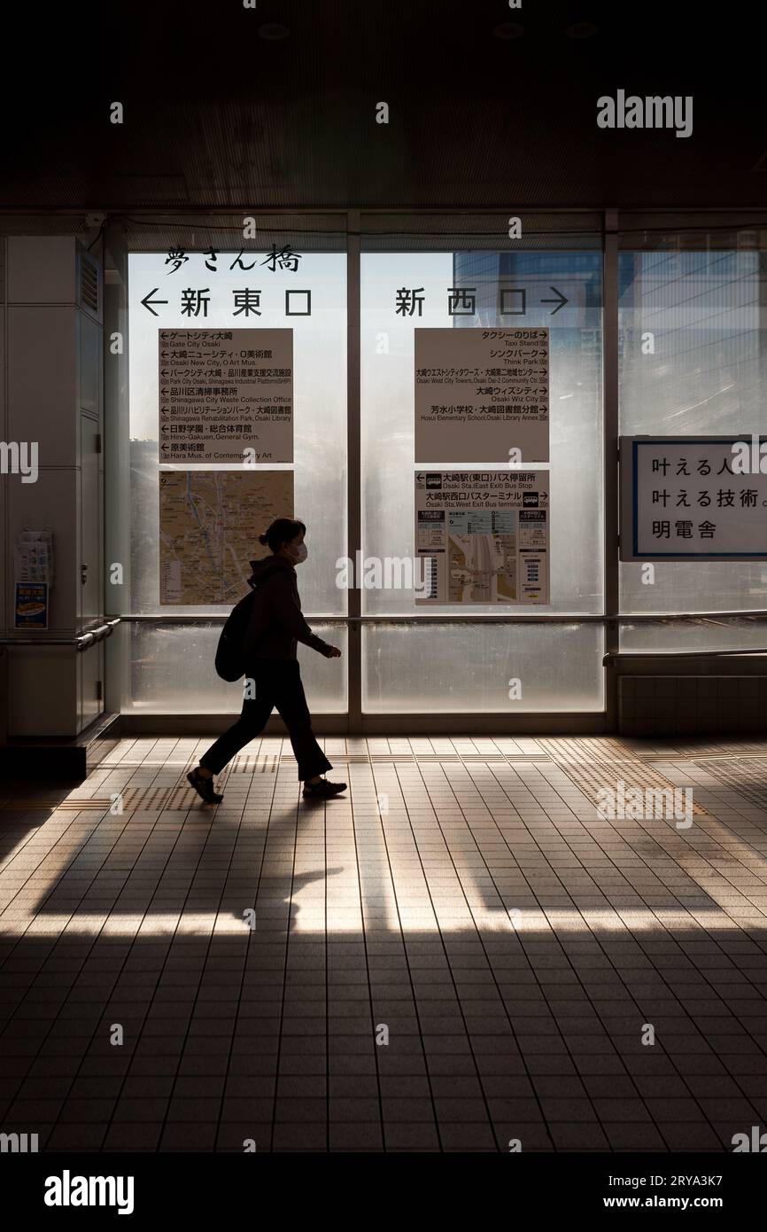 Silhouette of a woman wearing a face mask, walking through Osaki ...
