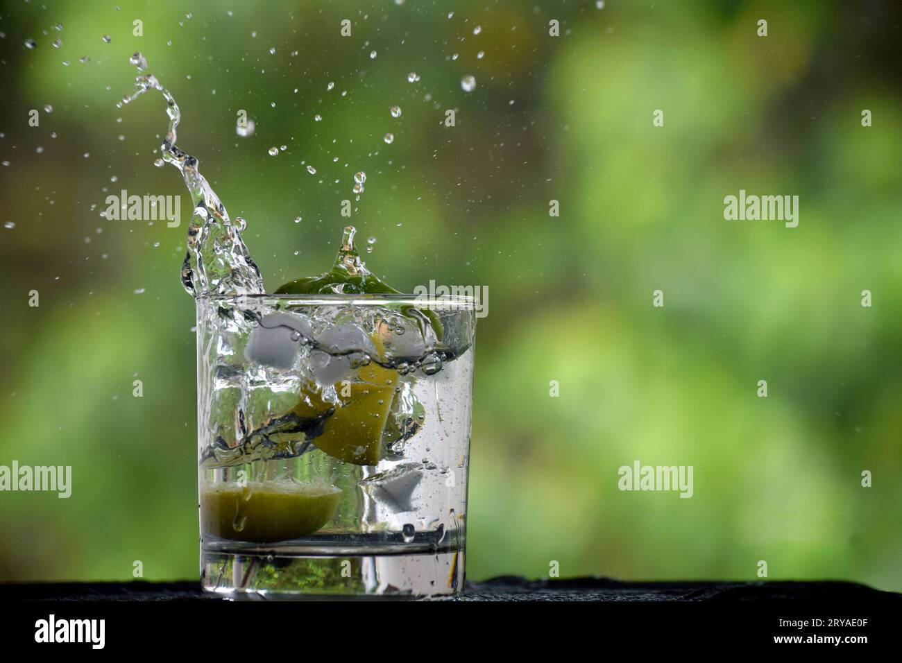 Preparing lemonade drink. Lemon pieces falling into water and soda ...