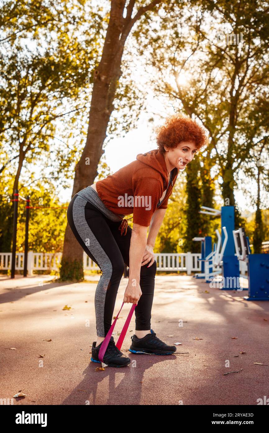Adult Caucasian woman does stretching with elastic band on street ...