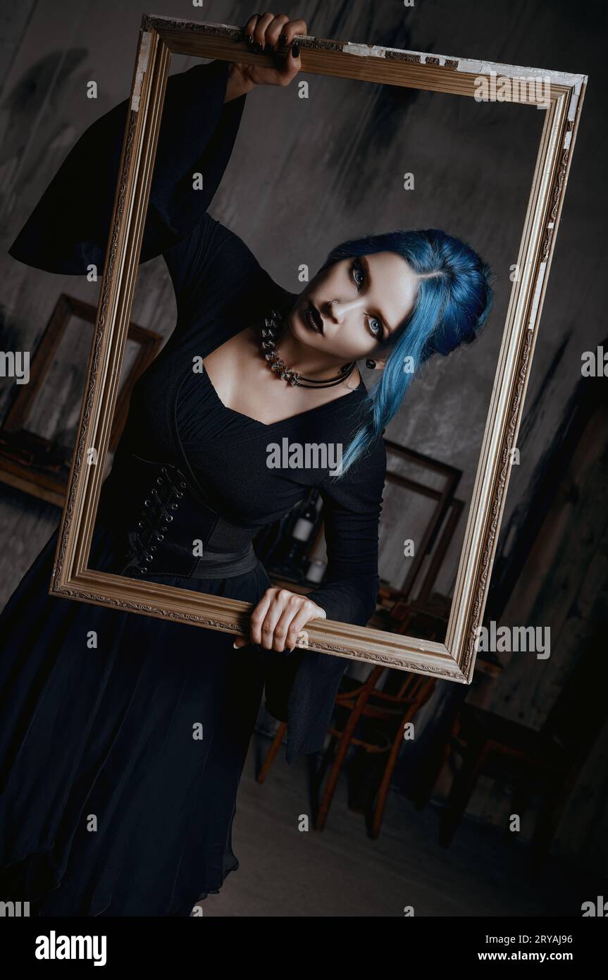 Indoors portrait of gorgeous goth girl in black dress. Blue-haired gothic lady holds a picture ...