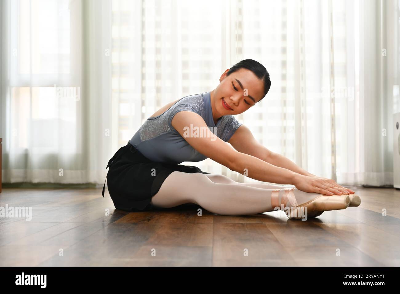 Young asian female ballet dancer stretching on floor in light ballet ...