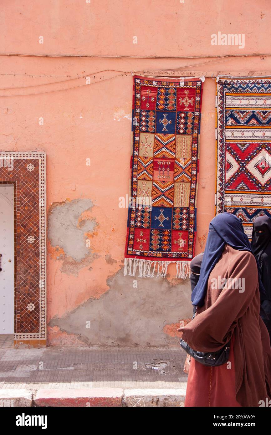 ladies in Hijab walk past hanging rugs in the streets of Marrakech ...