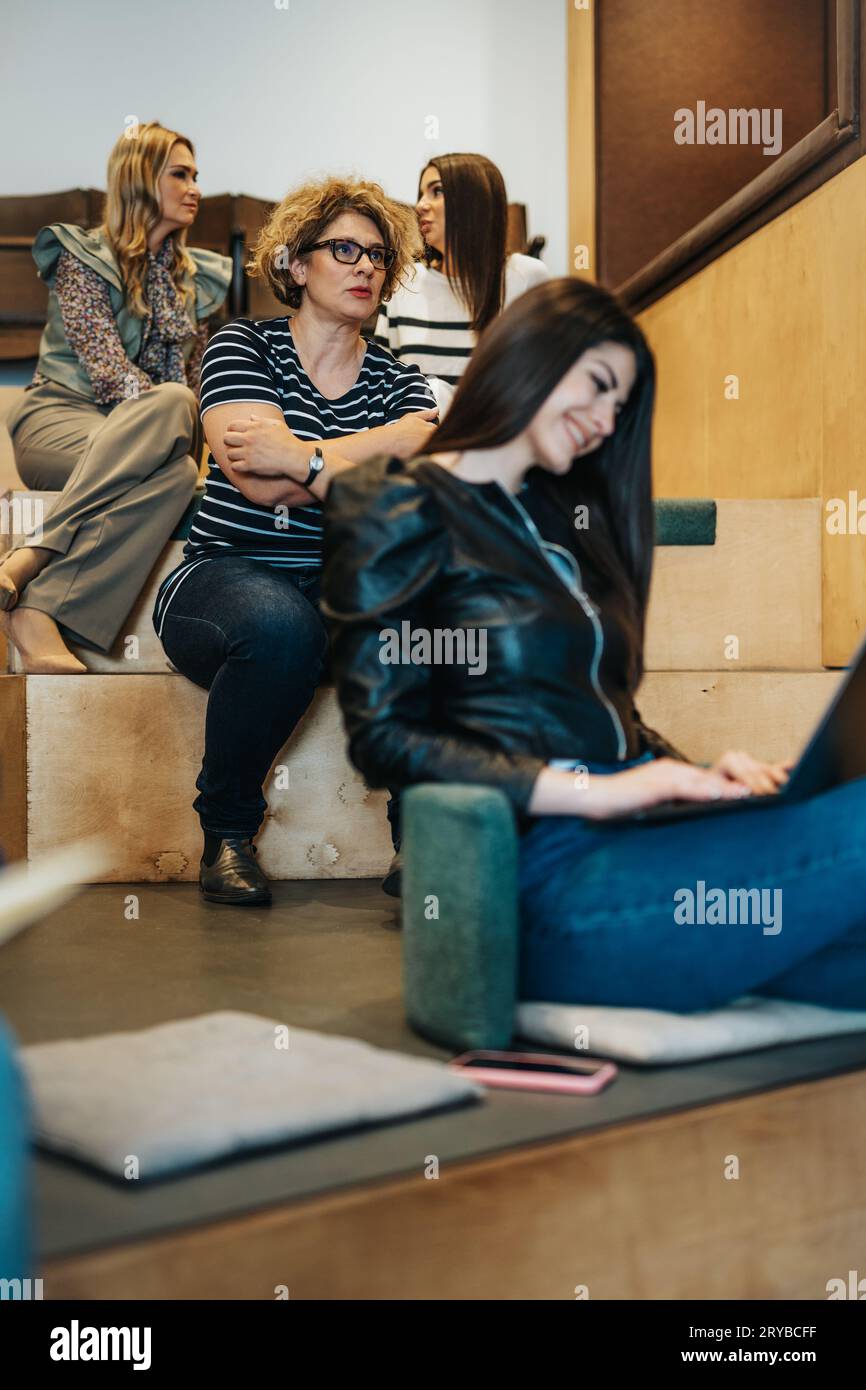 Adult female businessperson sat in the amphitheater with her colleagues ...