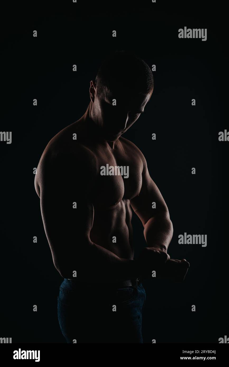 Stunning and well-built man standing in a dark room and flexing his ...