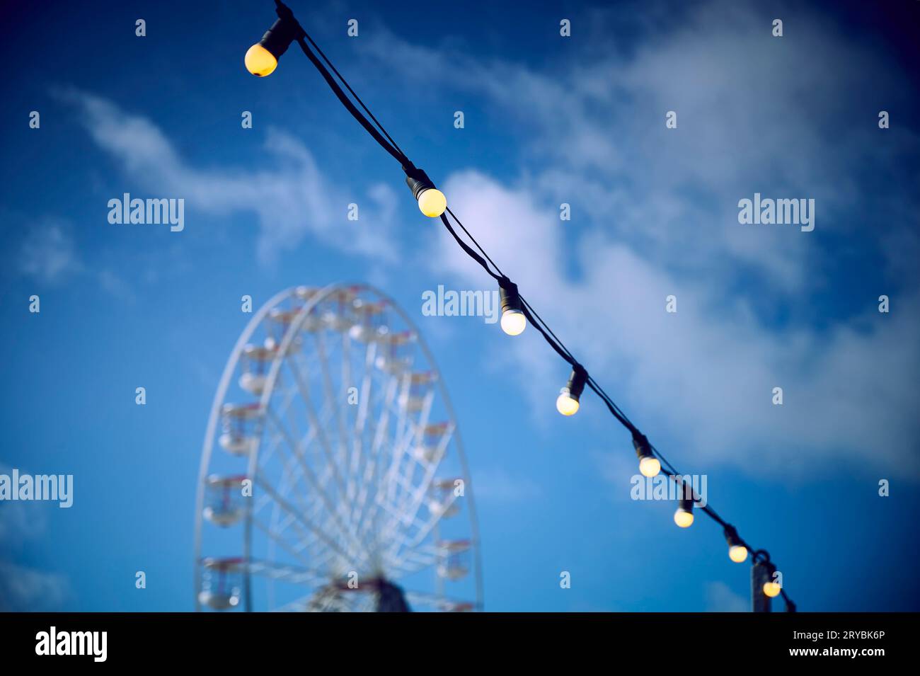 String of yellow light bulbs and Ferris wheel at dusk during Blackpool ...