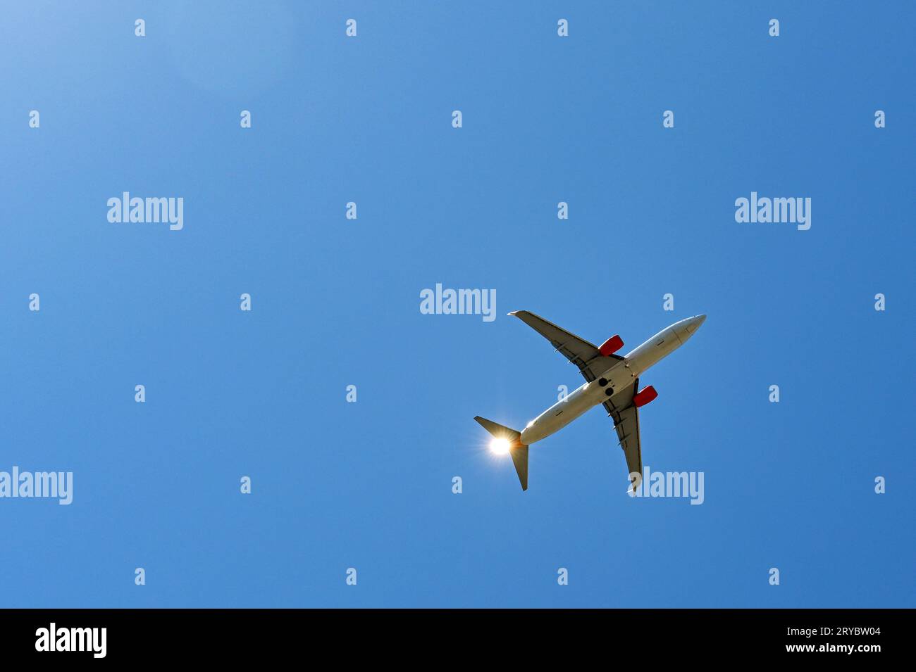 Modern passenger jet in flight isolated against a blue sky with the sun ...