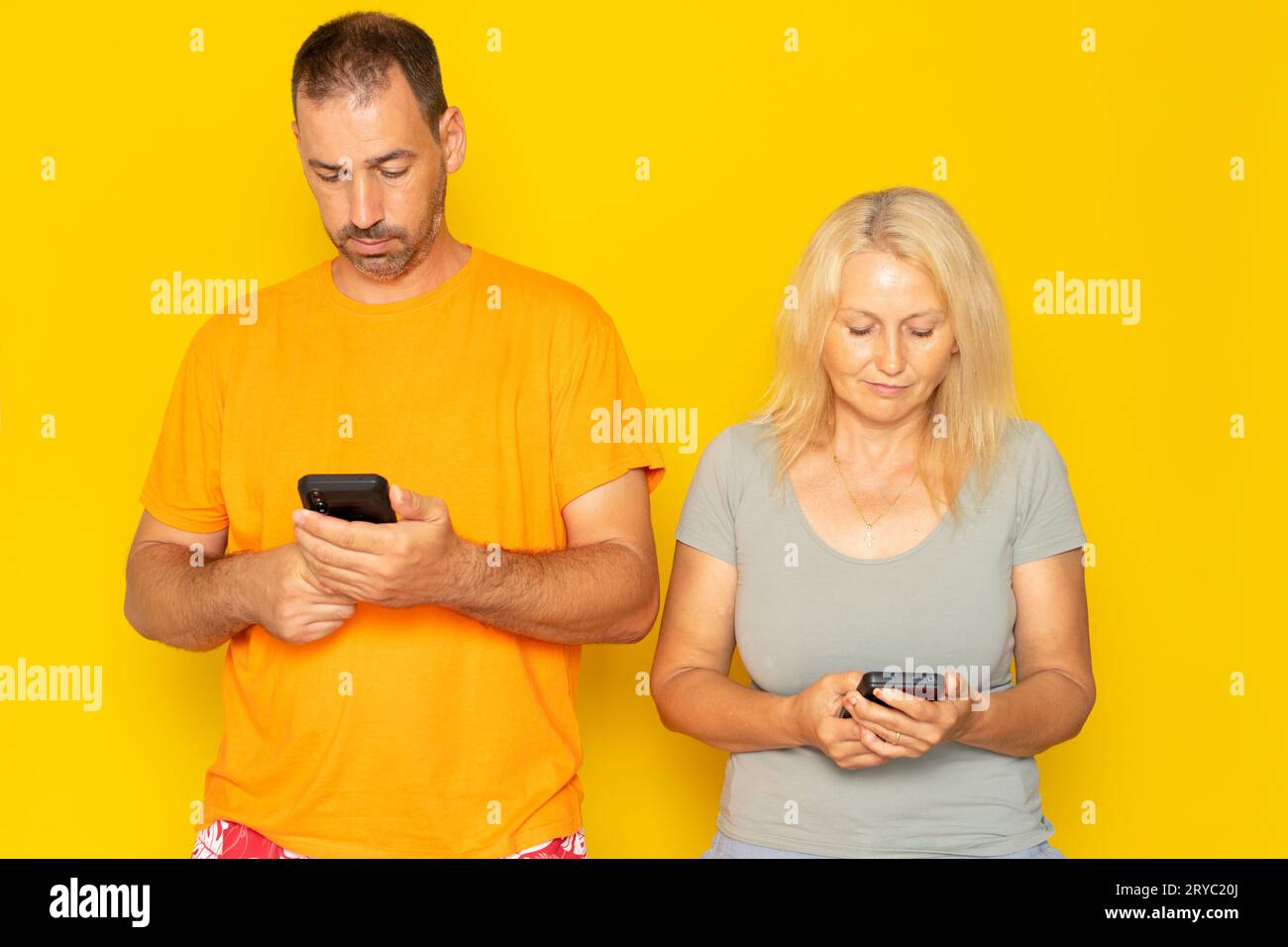 Middle aged couple looking at their cell phone ignoring each other ...