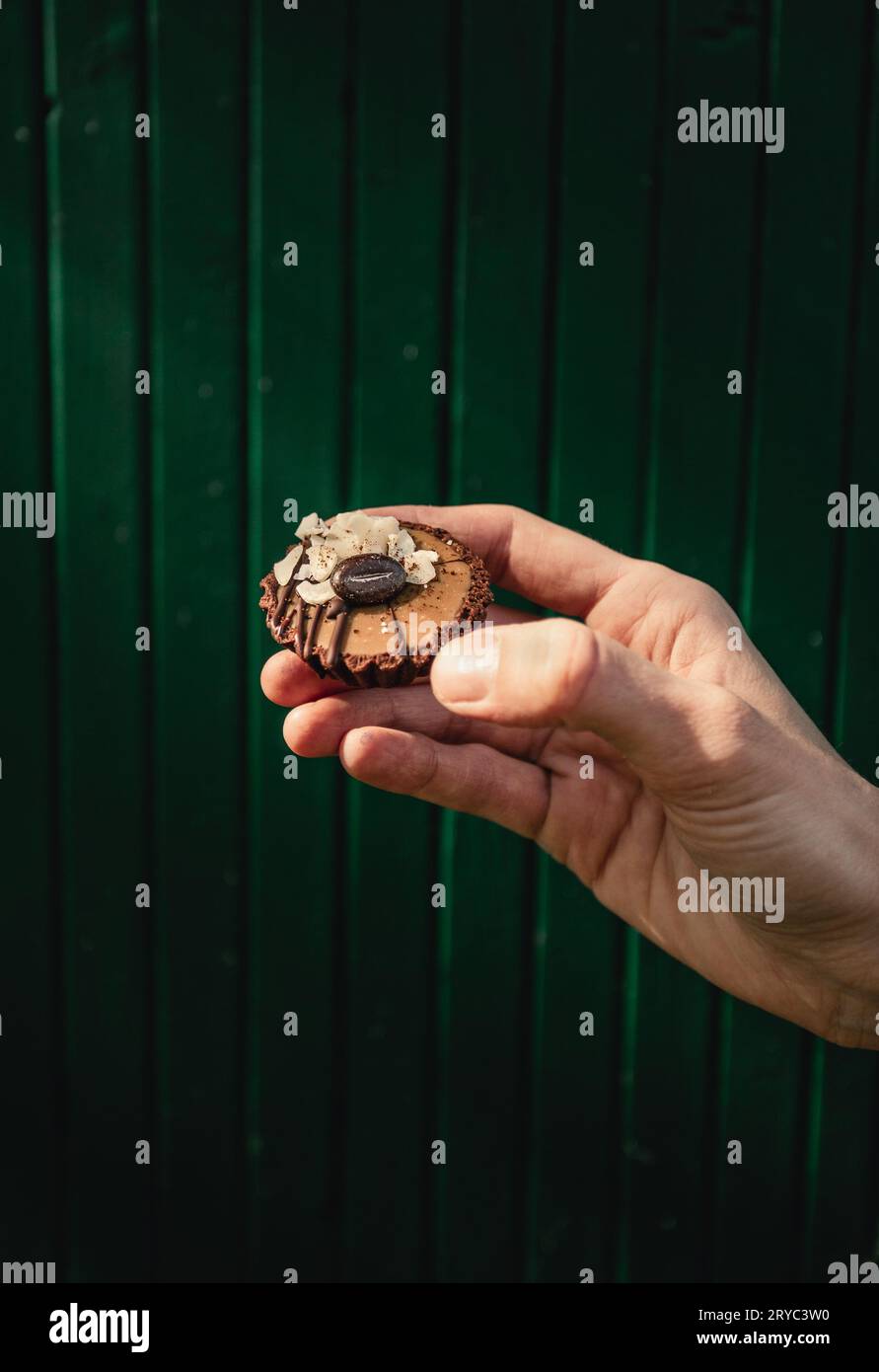 Female holding a cake in hand - green and dark background. Small tasty ...