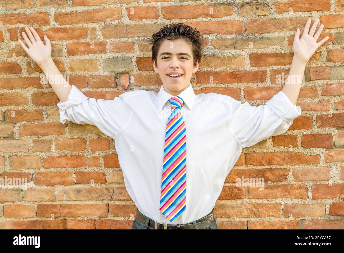 Handsome boy raising arms in front of a brick wall Stock Photo - Alamy