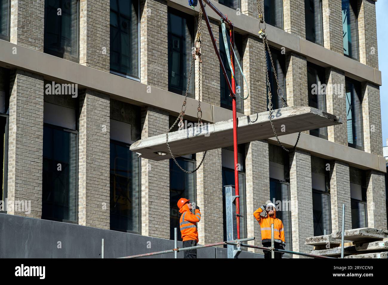 Two construction workers supervise a concrete slab being lowered into ...