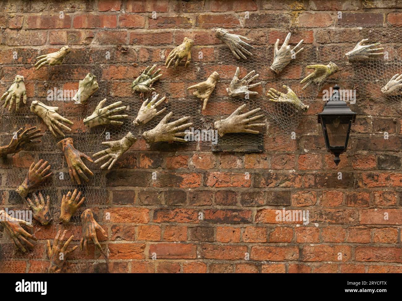 Red brick wall with multiple manaking hands attached using chicken wire ...