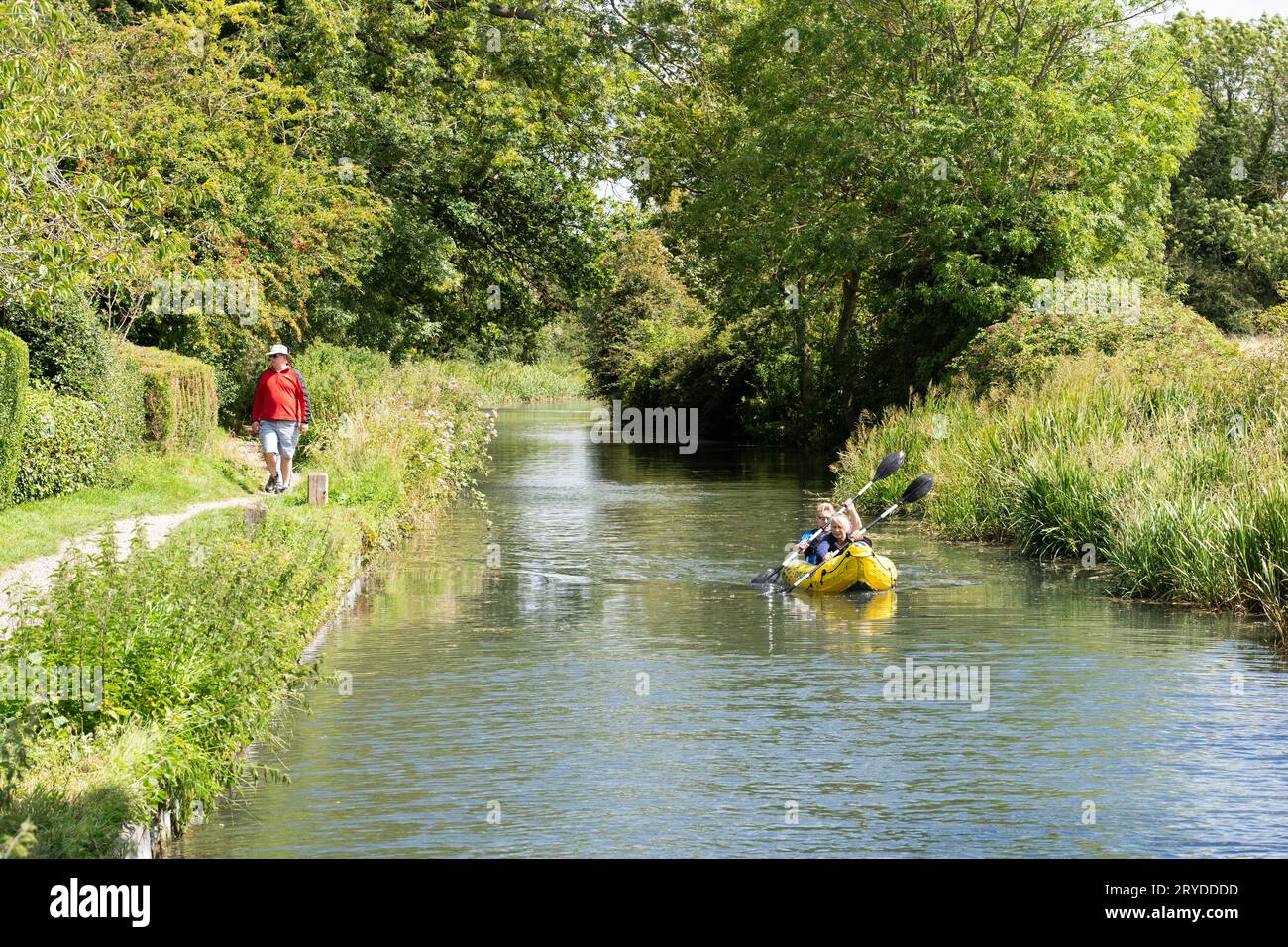 A man walking along a canal path with a man and a woman paddling in a ...