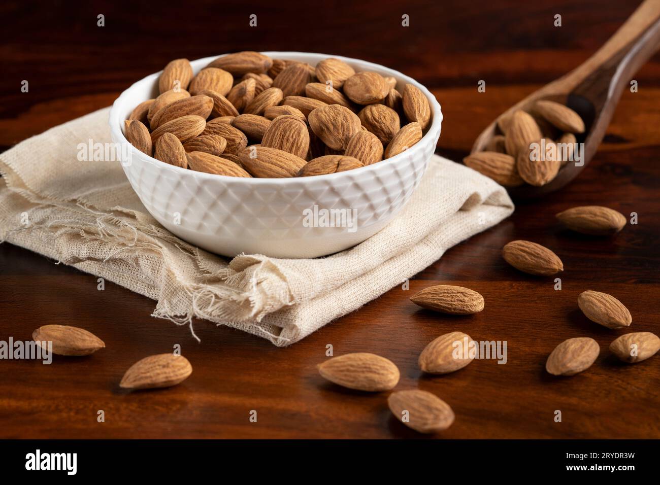 A white bowl full of organic almonds kept on white cotton cloth and ...