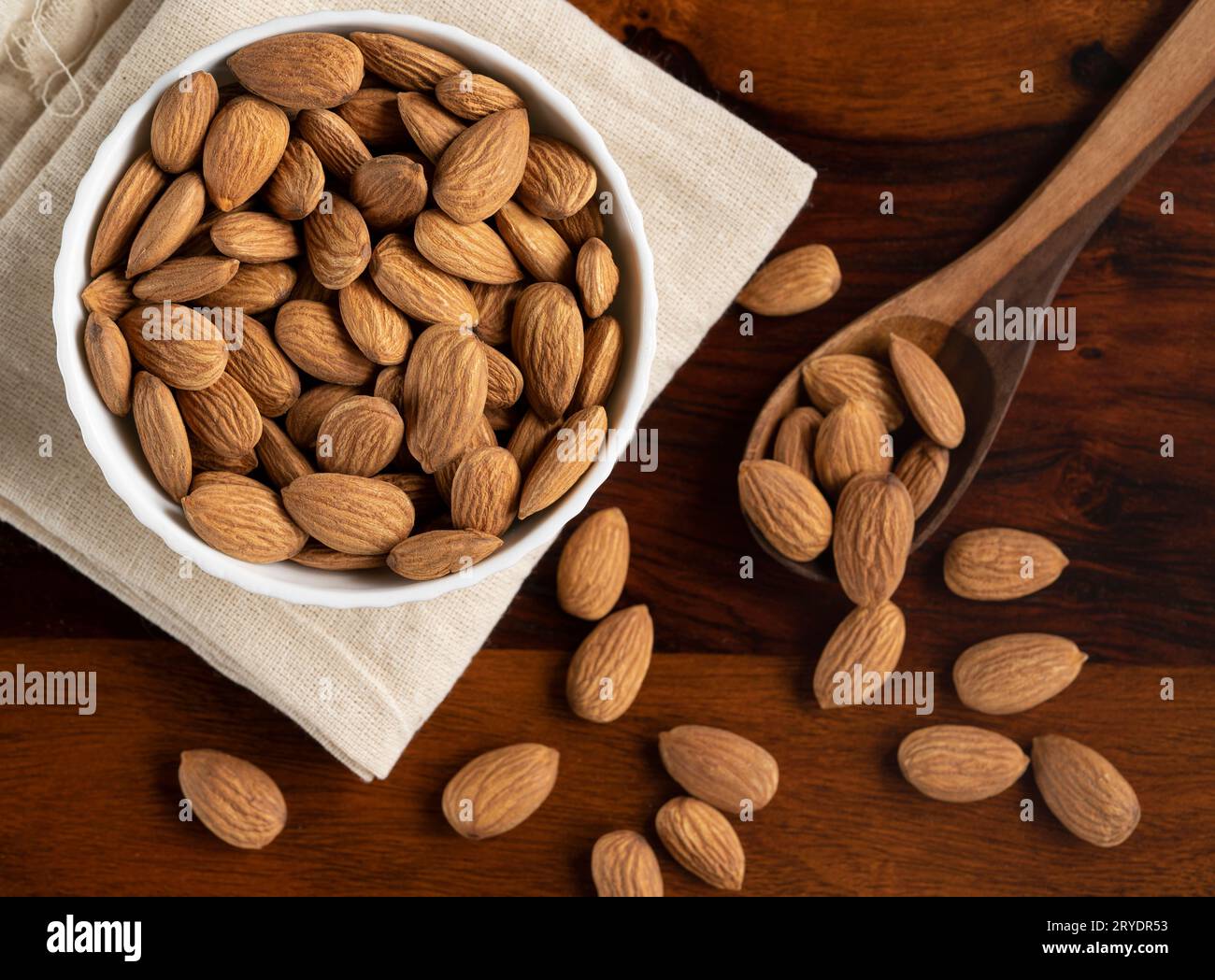 A white bowl full of organic almonds kept on white cotton cloth and ...
