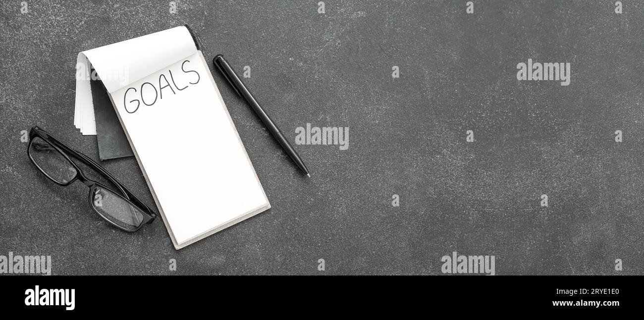 Notebook with word GOALS, pen and eyeglasses on dark grunge background ...