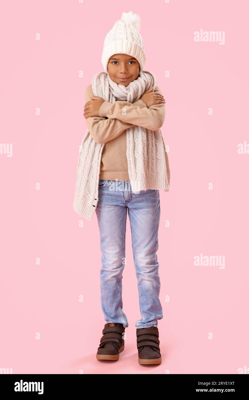 Freezing African-American boy in winter clothes on pink background ...