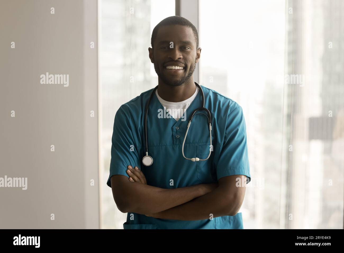 Happy handsome African American surgeon in blue scrubs standing indoors ...