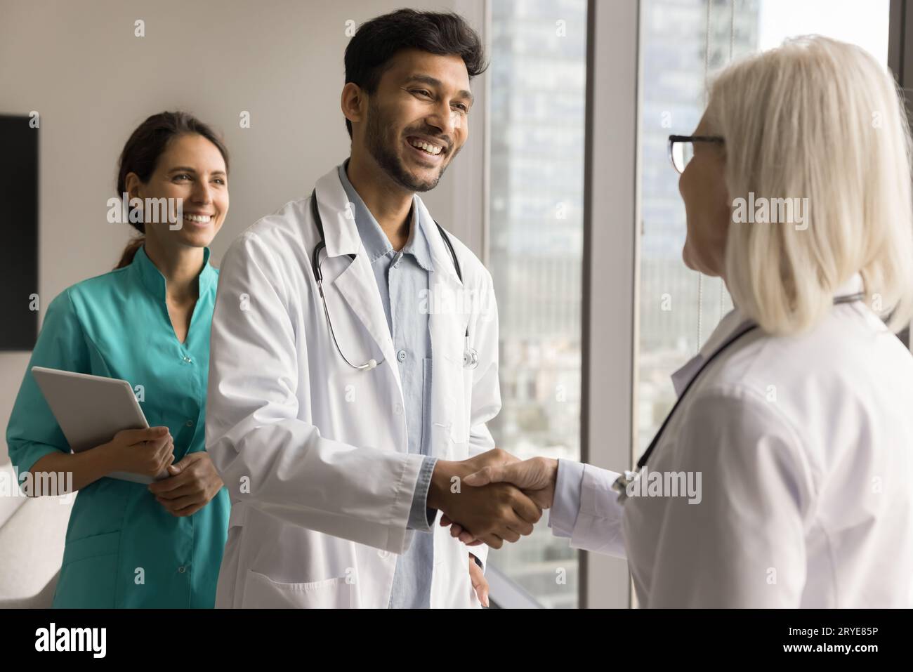 Clinic mature head doctor congratulating younger Indian intern on ...