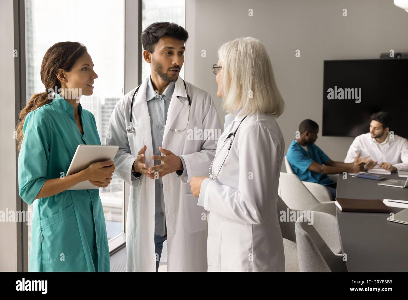 Diverse group of practitioners in uniform coats discussing medical ...