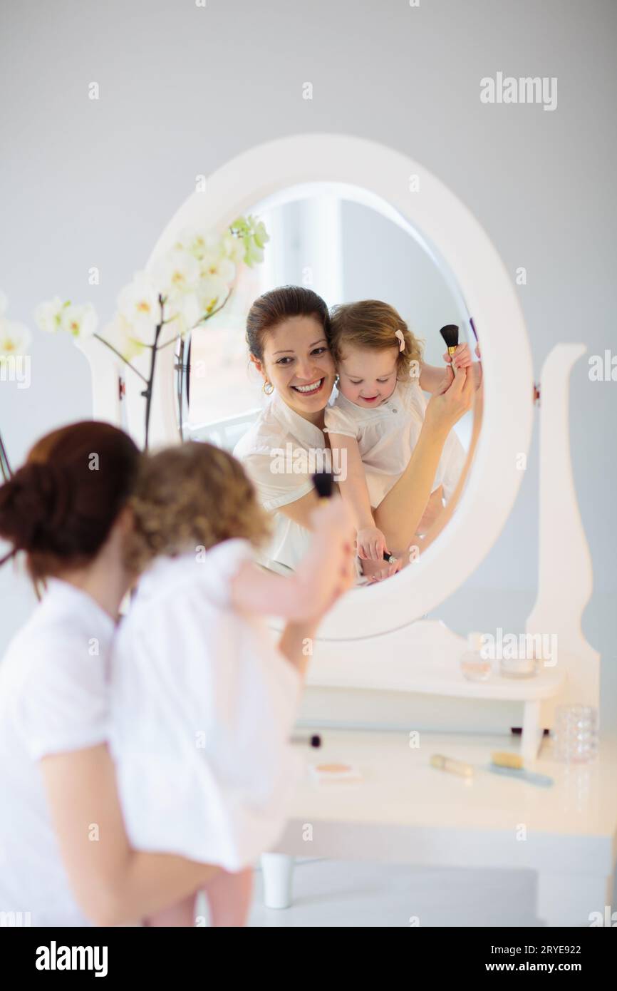 Mother and daughter looking in mirror. Young mom and little girl apply ...