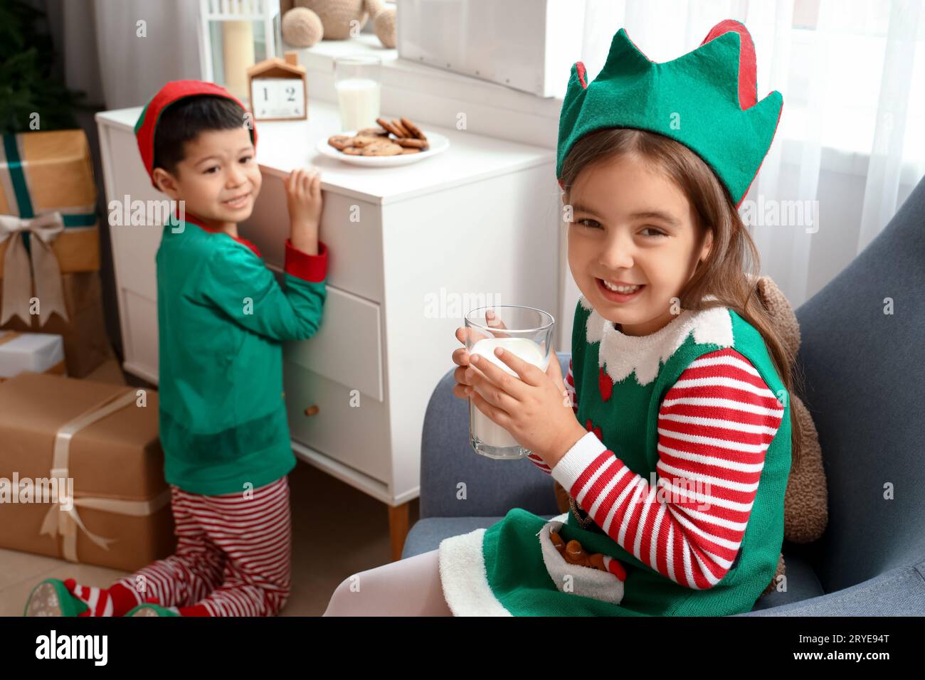 Cute little children dressed as elves with milk and cookies at home on ...