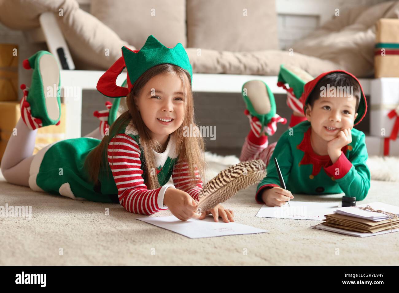 Cute little children dressed as elves writing letters to Santa at home ...