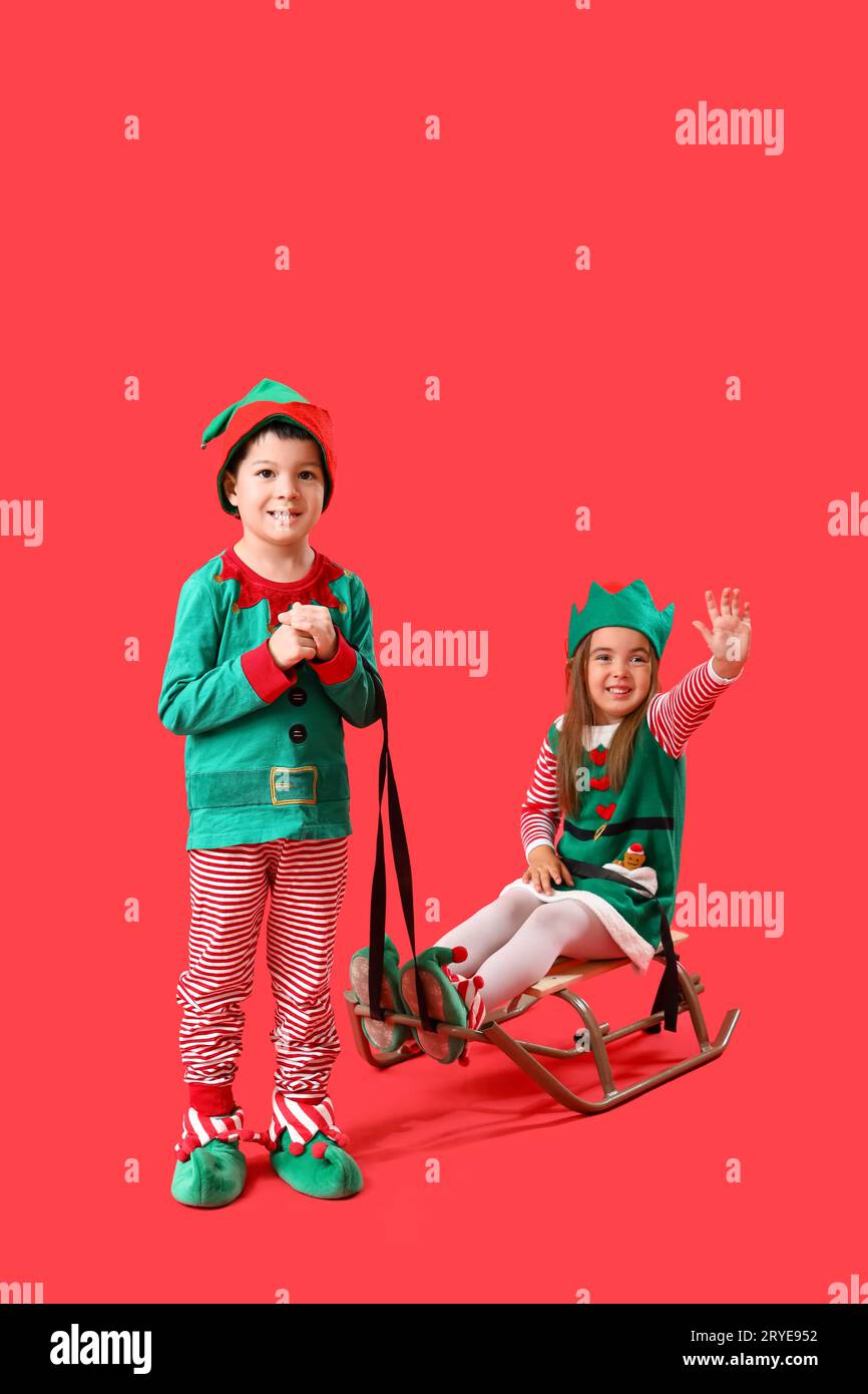 Cute little children dressed as elves with sledge on red background ...