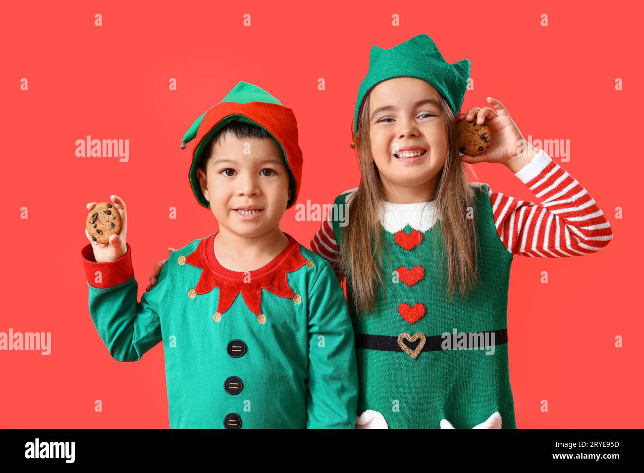 Cute little children dressed as elves with cookies on red background ...
