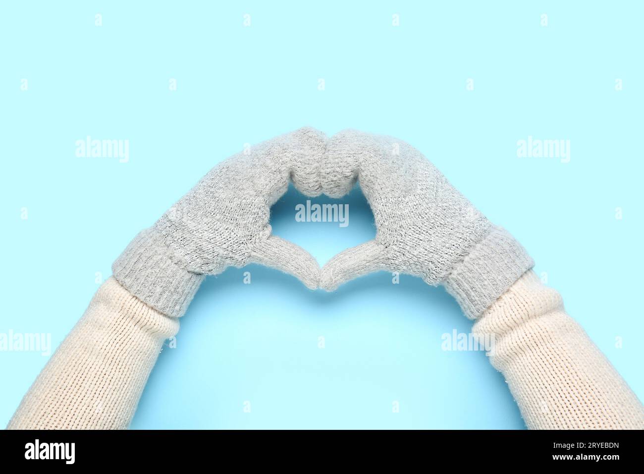 Woman in warm mittens making heart shape with her hands on color ...