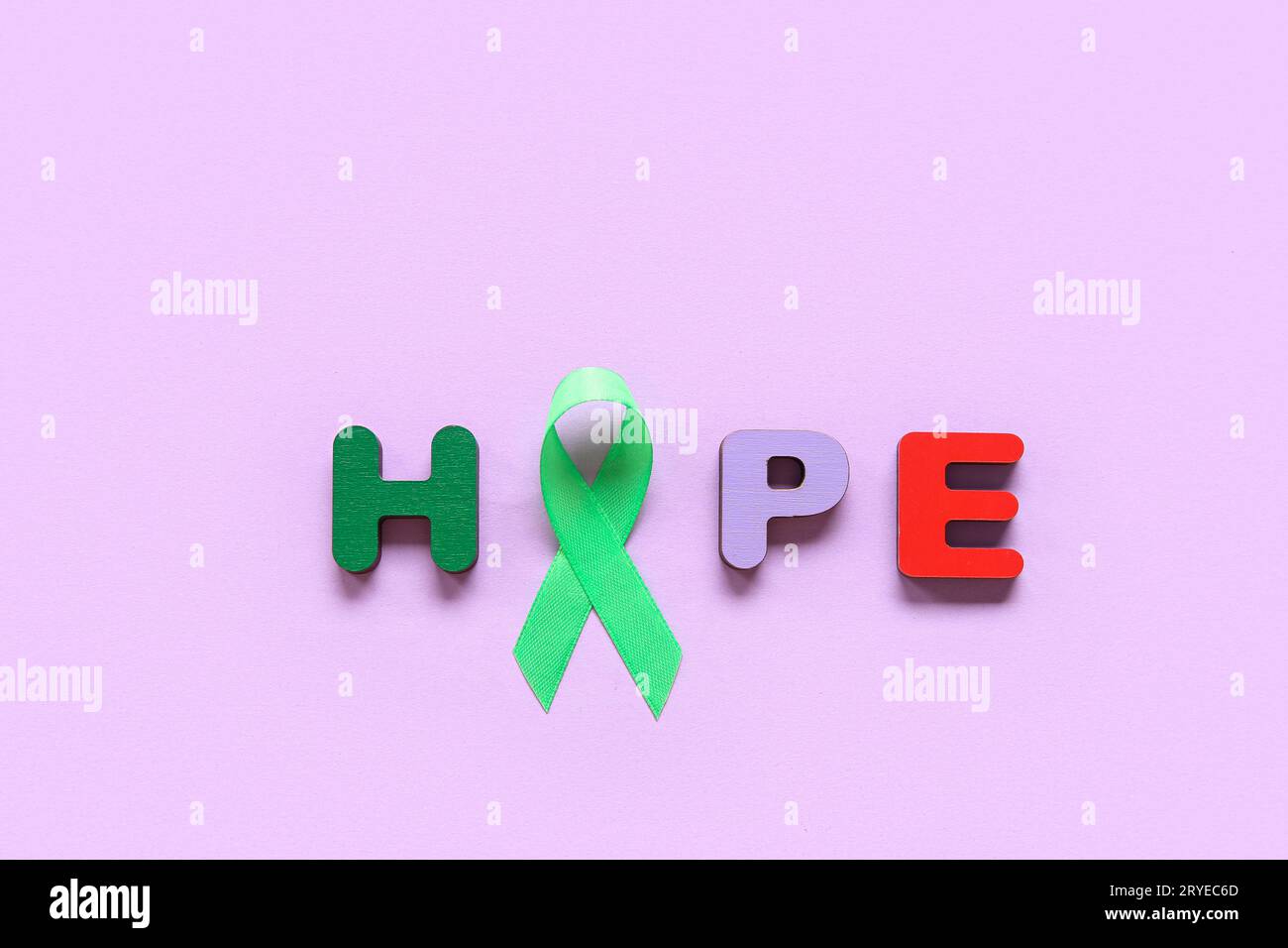 Green awareness ribbon and word HOPE made of wooden letters on purple ...