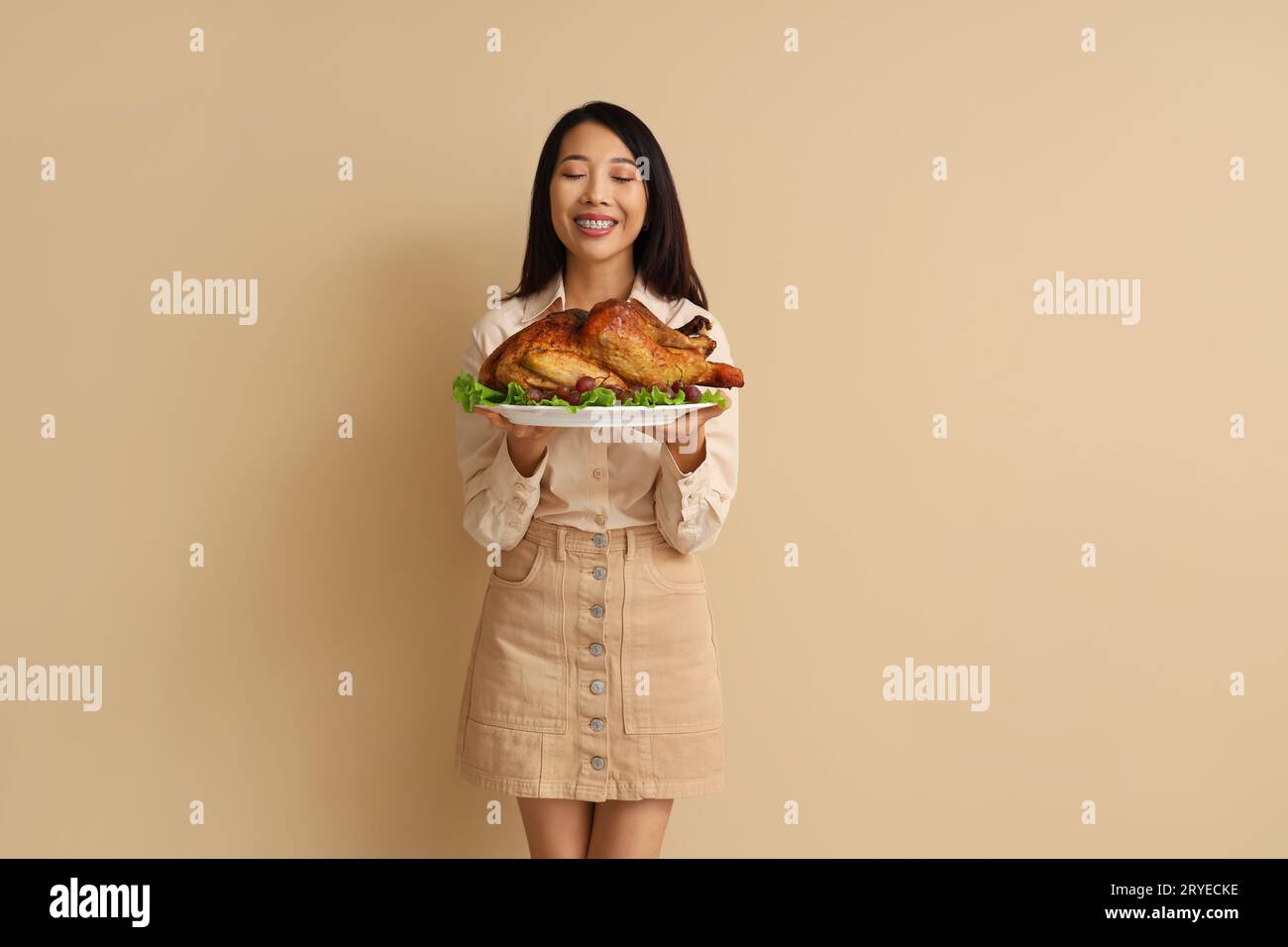 Young Asian woman with tasty turkey on beige background. Thanksgiving ...