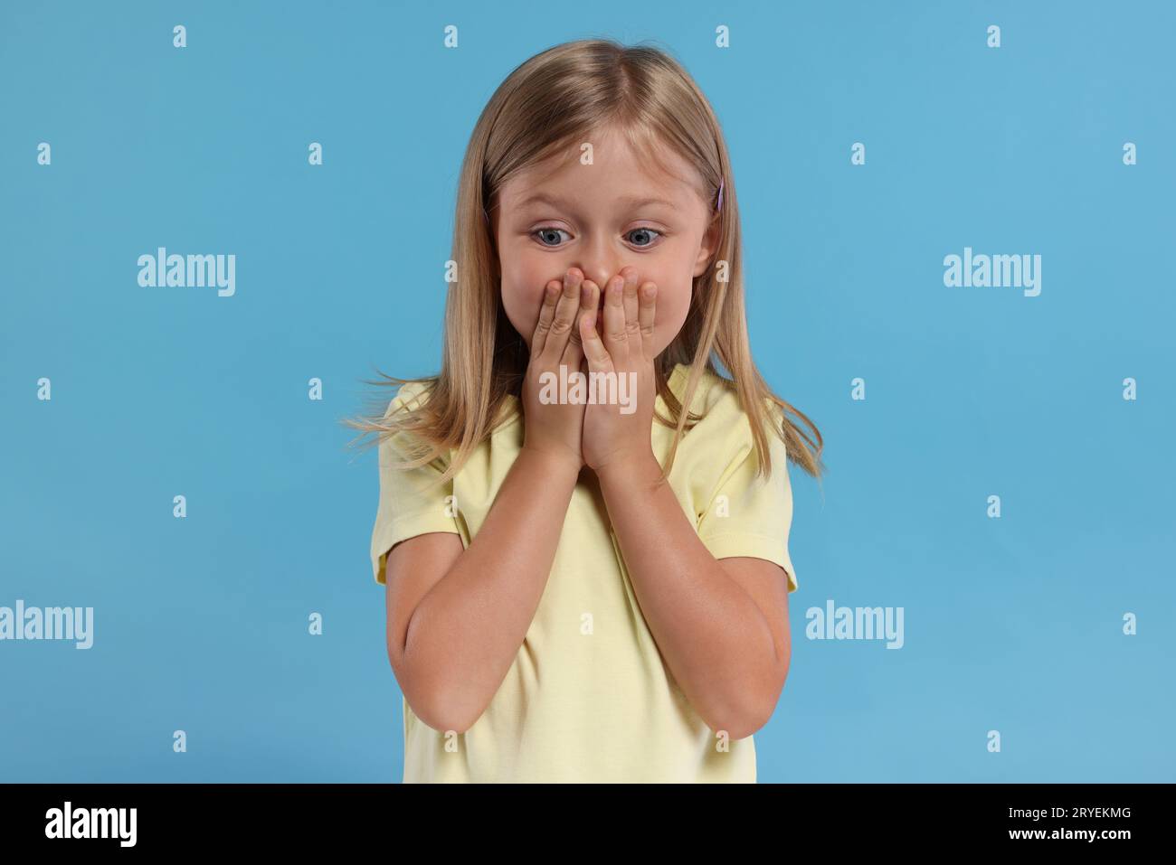 Embarrassed little girl covering mouth with hands on light blue ...