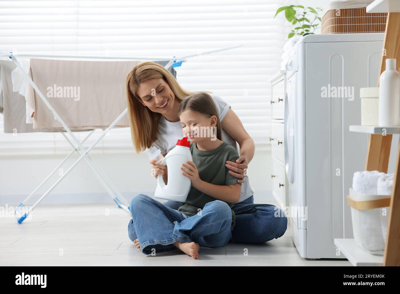 Mother and daughter sitting on floor near clothes dryer and smelling ...