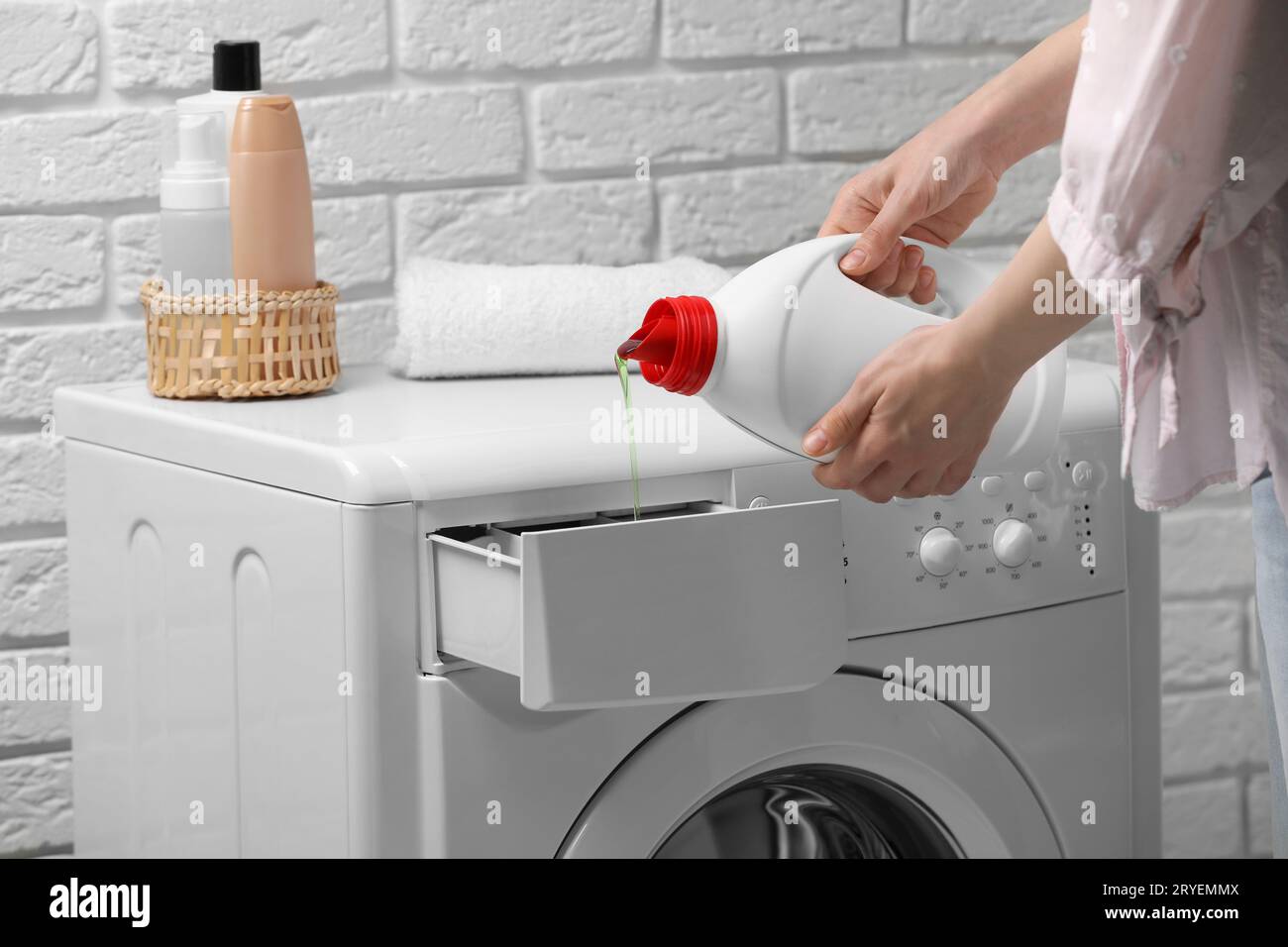 Woman pouring fabric softener from bottle into washing machine near ...