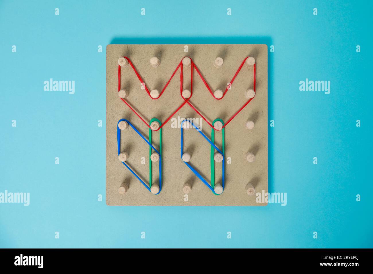 Wooden geoboard with flower shapes made of rubber bands on light blue ...