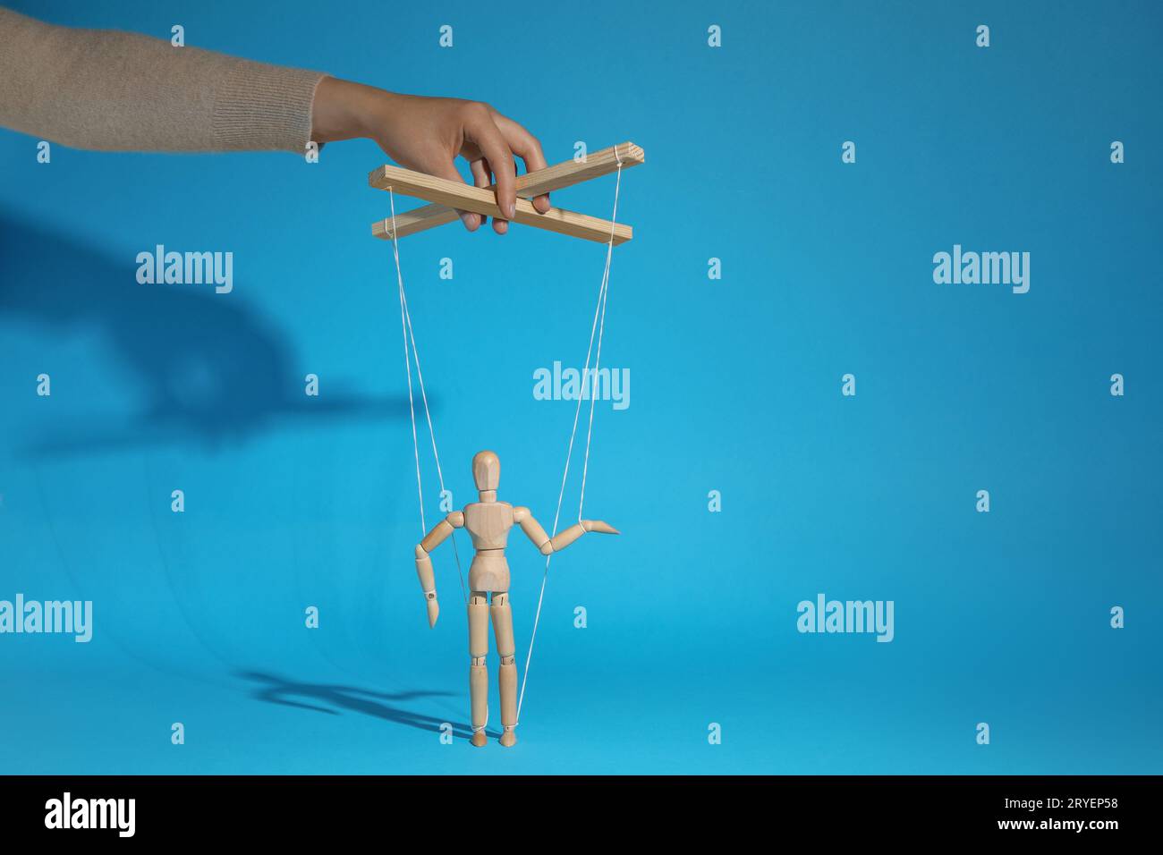 Woman pulling strings of puppet on light blue background, closeup Stock ...