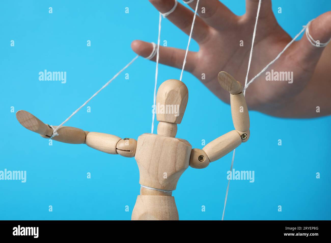 Woman pulling strings of puppet on light blue background, closeup Stock ...