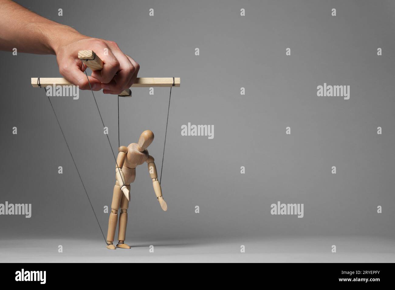 Man pulling strings of puppet on gray background, closeup. Space for ...