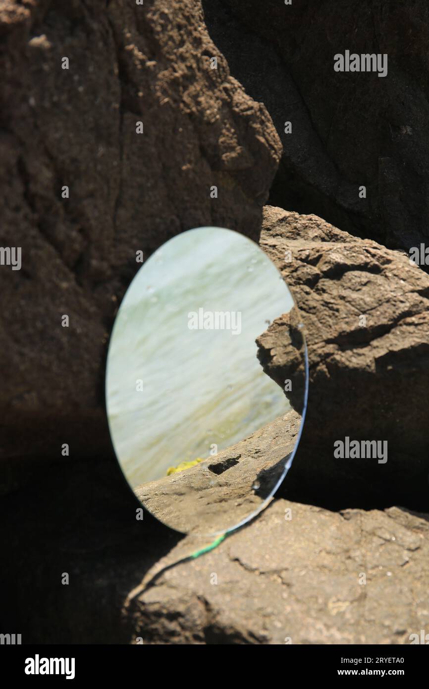Round mirror reflecting sea on stones outdoors Stock Photo - Alamy