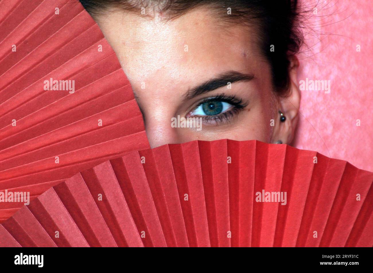 Face of a woman behind red hand fans Stock Photo - Alamy