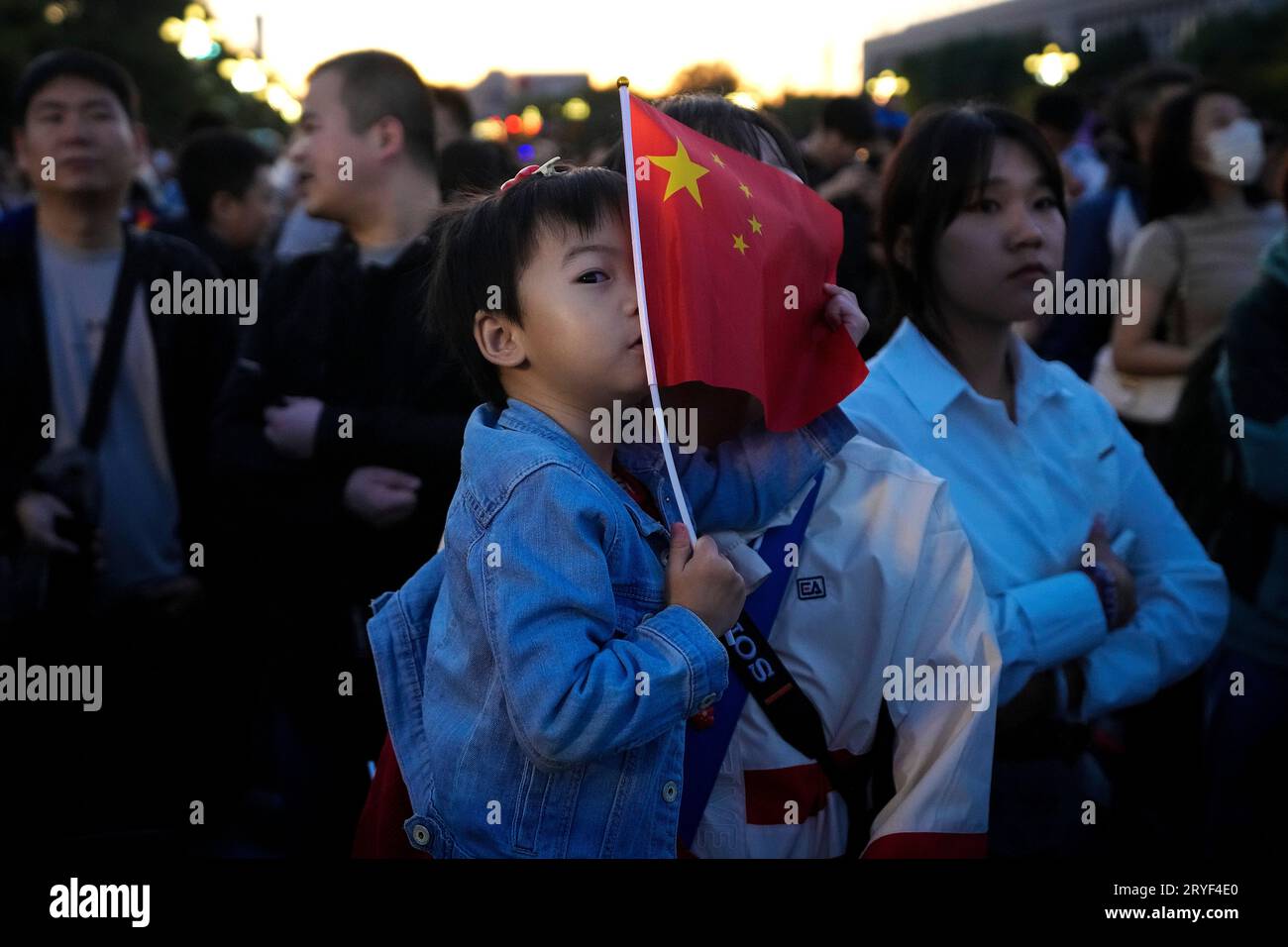 A child peeps from behind a national flag as people gather on a street ...