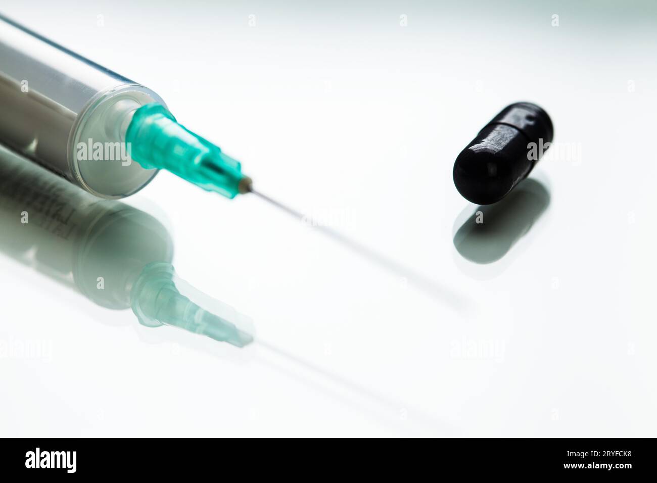 Green needle in syringe and black pill medication on white reflective ...