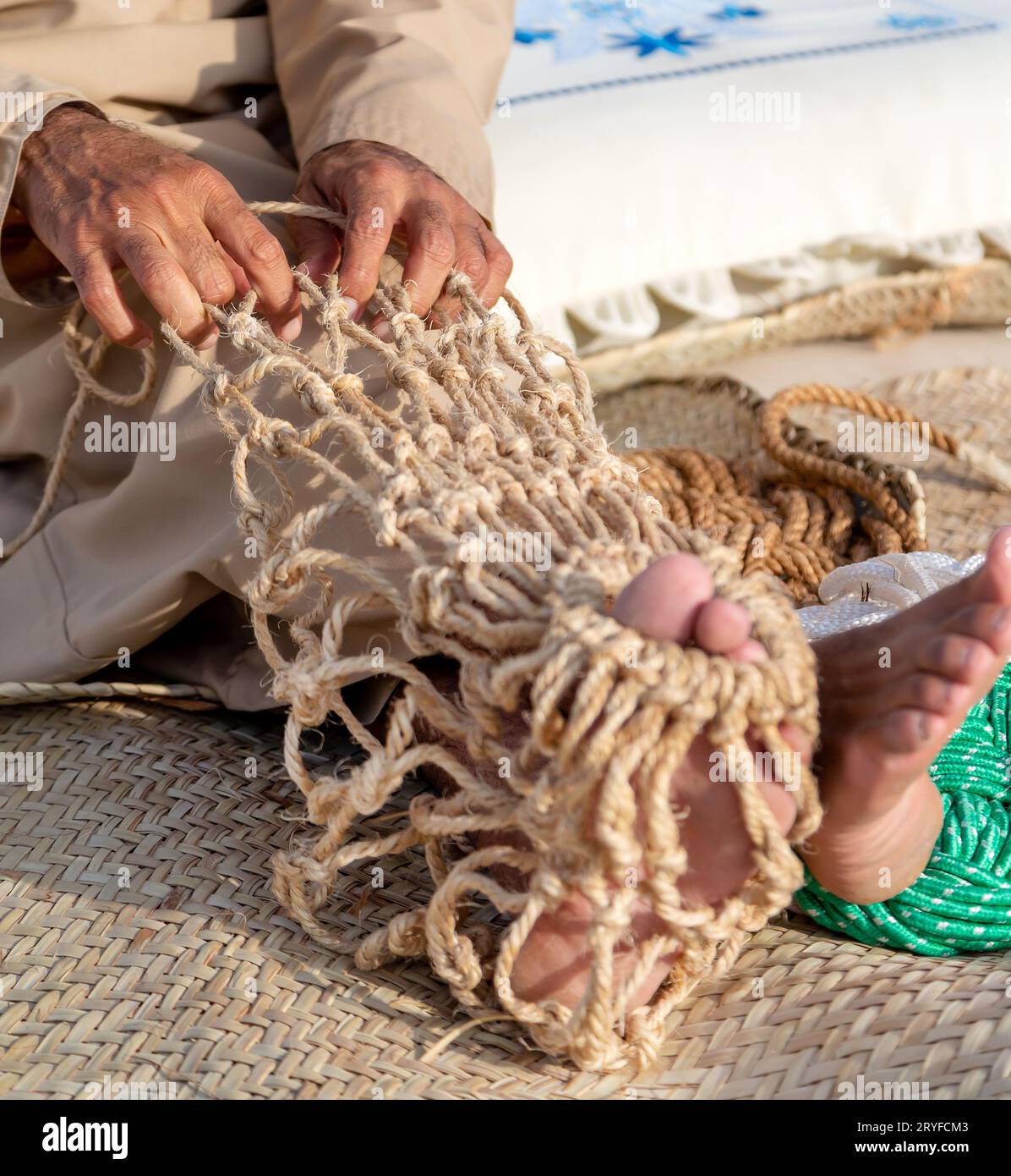 Old man is knitting traditional fishing net, hands and feet in frame ...